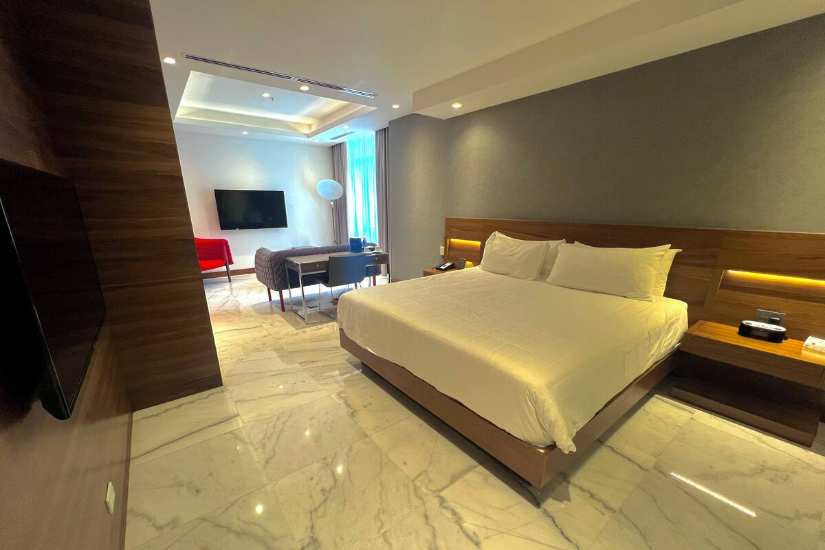 Quarto de hotel moderno com uma cama grande, uma escrivaninha e uma televisão.