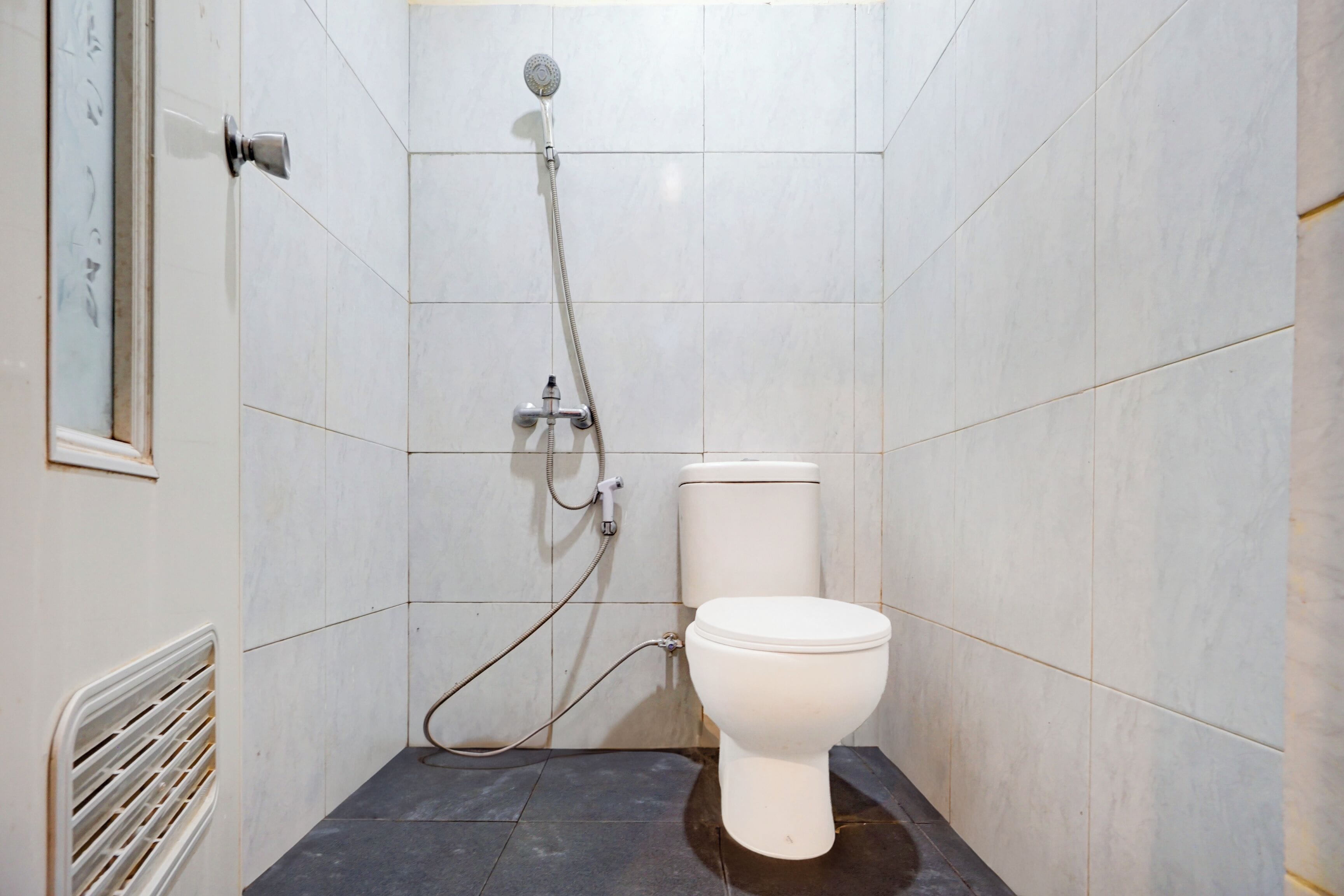 Uma casa de banho pequena e moderna, com chuveiro, sanita e ventilação na parede.