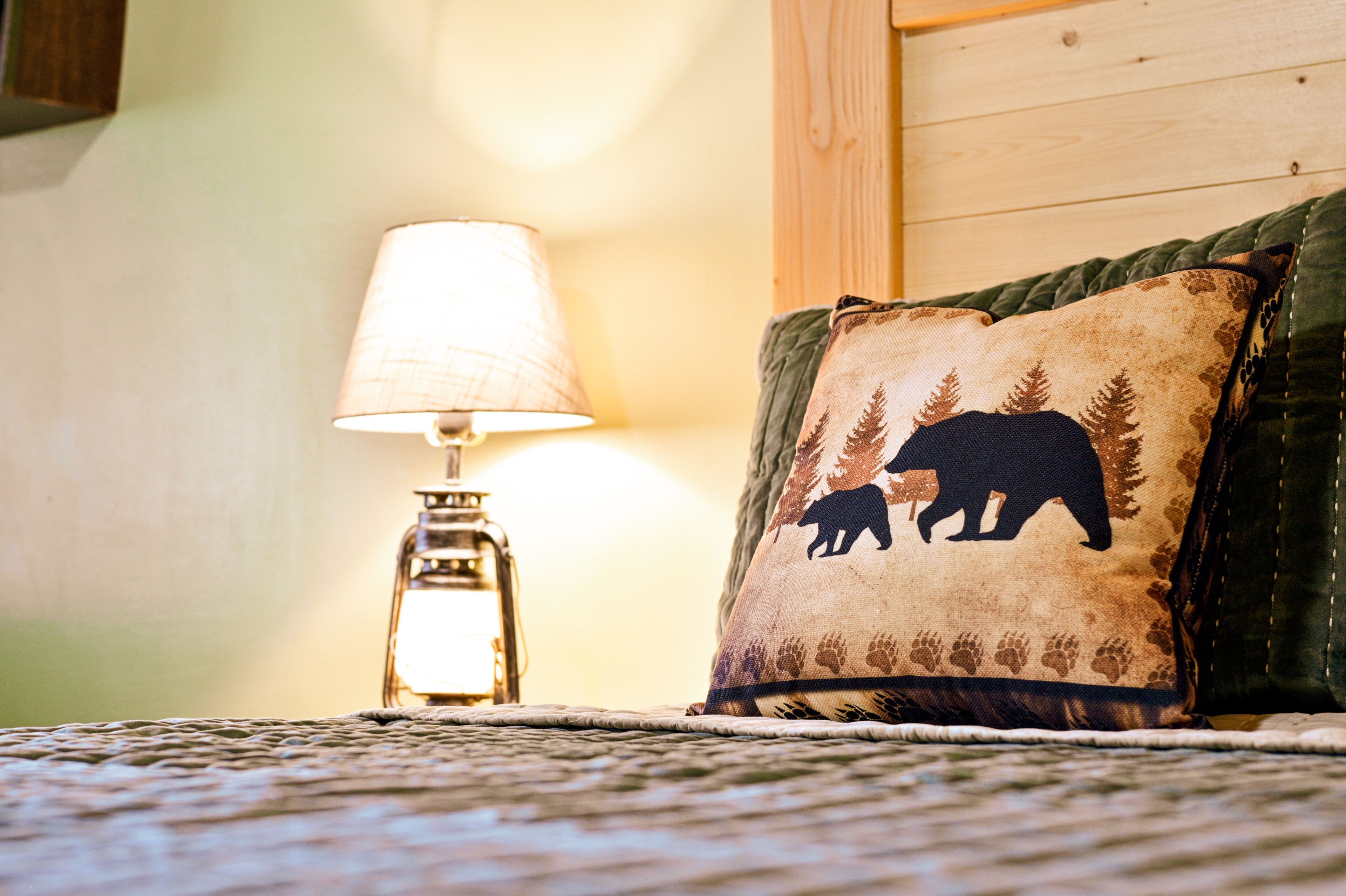 Cama com colcha verde e travesseiro com desenho de urso e pegadas.