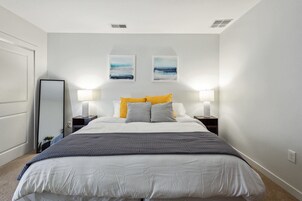 Quarto com cama, duas luminárias de cabeceira, um espelho e duas obras de arte na parede.