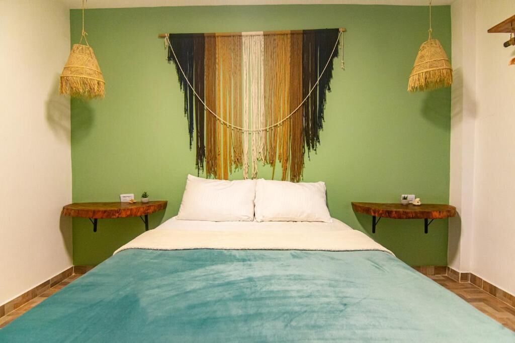 Quarto com uma cama, duas mesas de cabeceira, uma tapeçaria pendurada e duas luminárias.