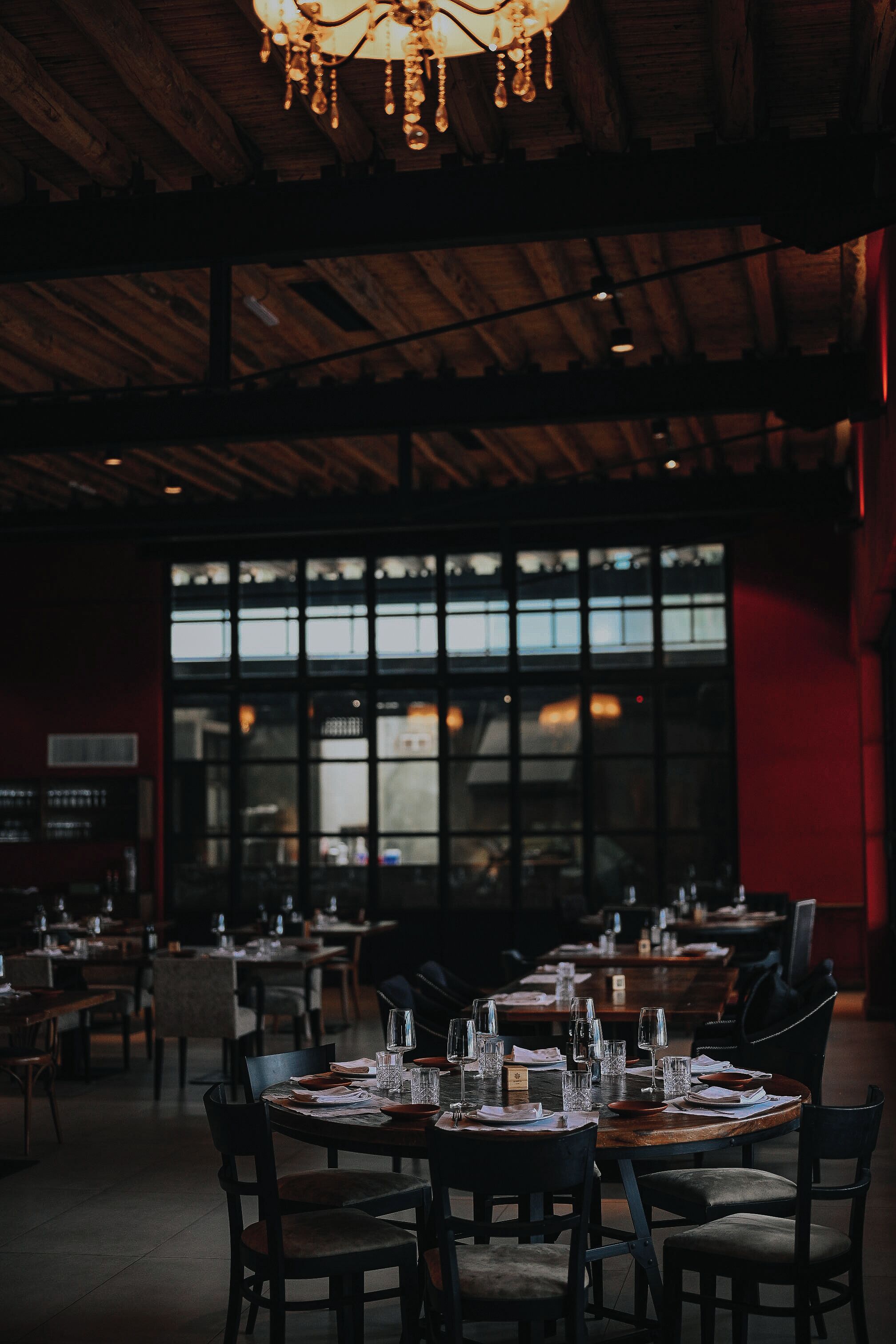 Restaurante com mesas preparadas para refeições, amplas janelas e teto de madeira.