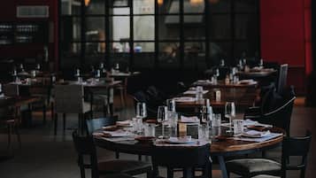 Restaurante com mesas preparadas para refeições, amplas janelas e teto de madeira.