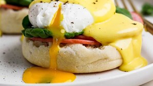 Prato de café da manhã com ovos pochê, molho holandês, espinafre e tomate sobre um prato branco.