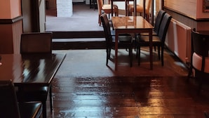 Interior de restaurante com chão de madeira, mesas, cadeiras, uma planta e luminárias pendentes.