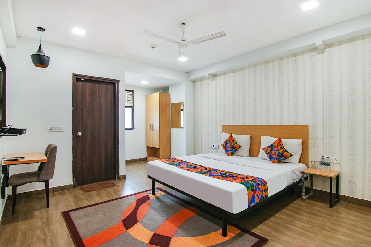 Quarto de hotel com cama, escrivaninha, cadeira, ventoinha no teto e janela com cortinas.
