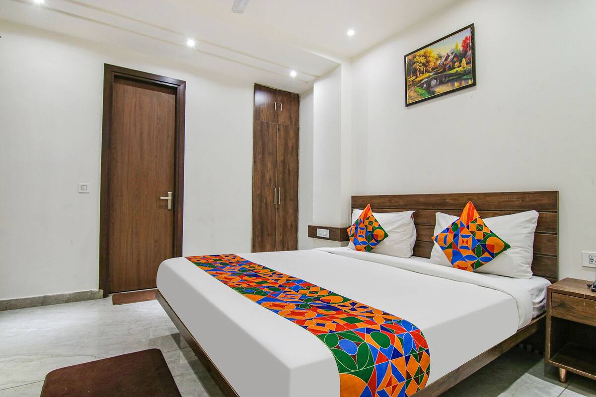 Quarto de hotel com uma cama grande, duas mesas de cabeceira, um guarda-roupa de madeira e um quadro na parede.