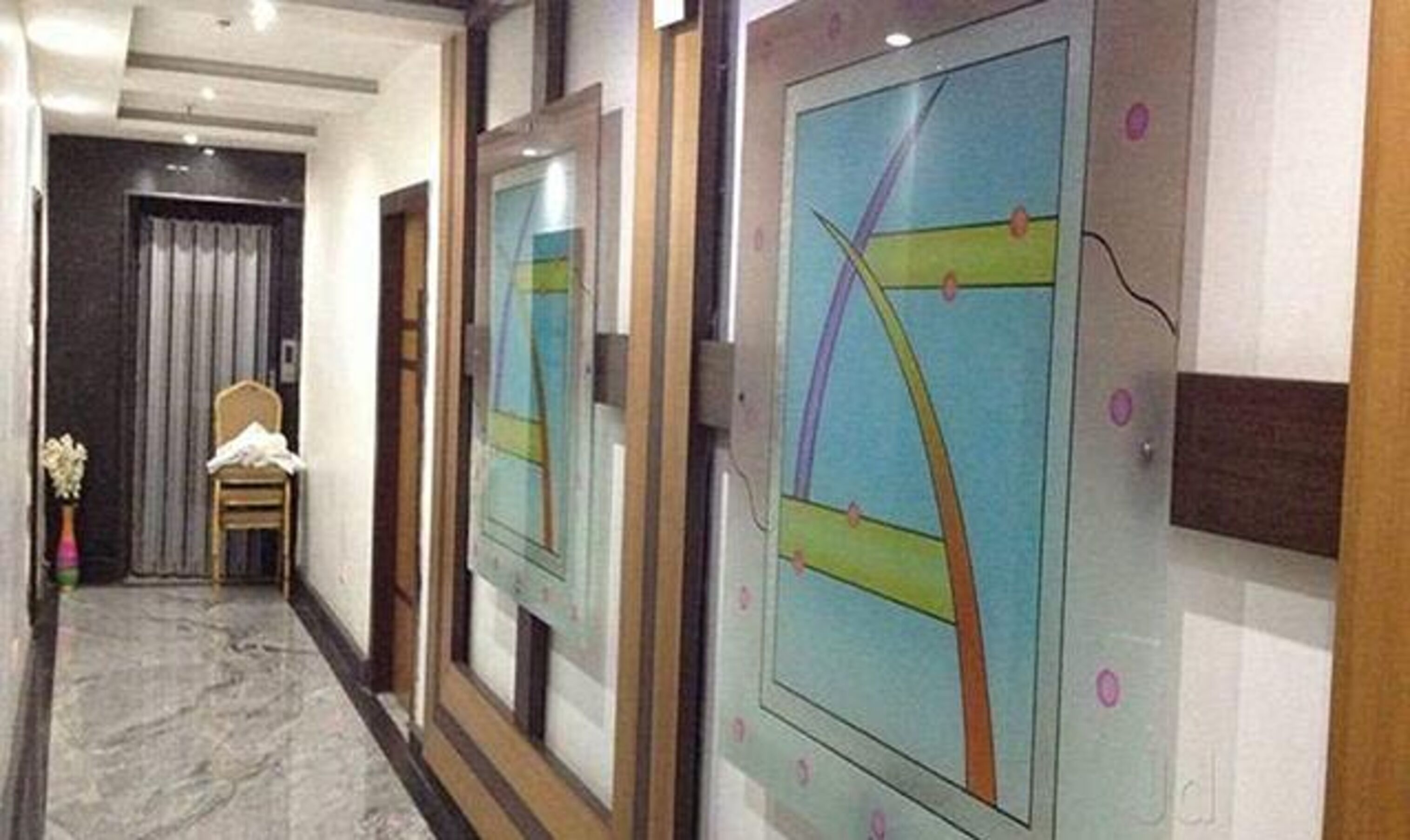Corredor de hotel com obras de arte emolduradas nas paredes, uma cadeira de madeira e um vaso com flores.