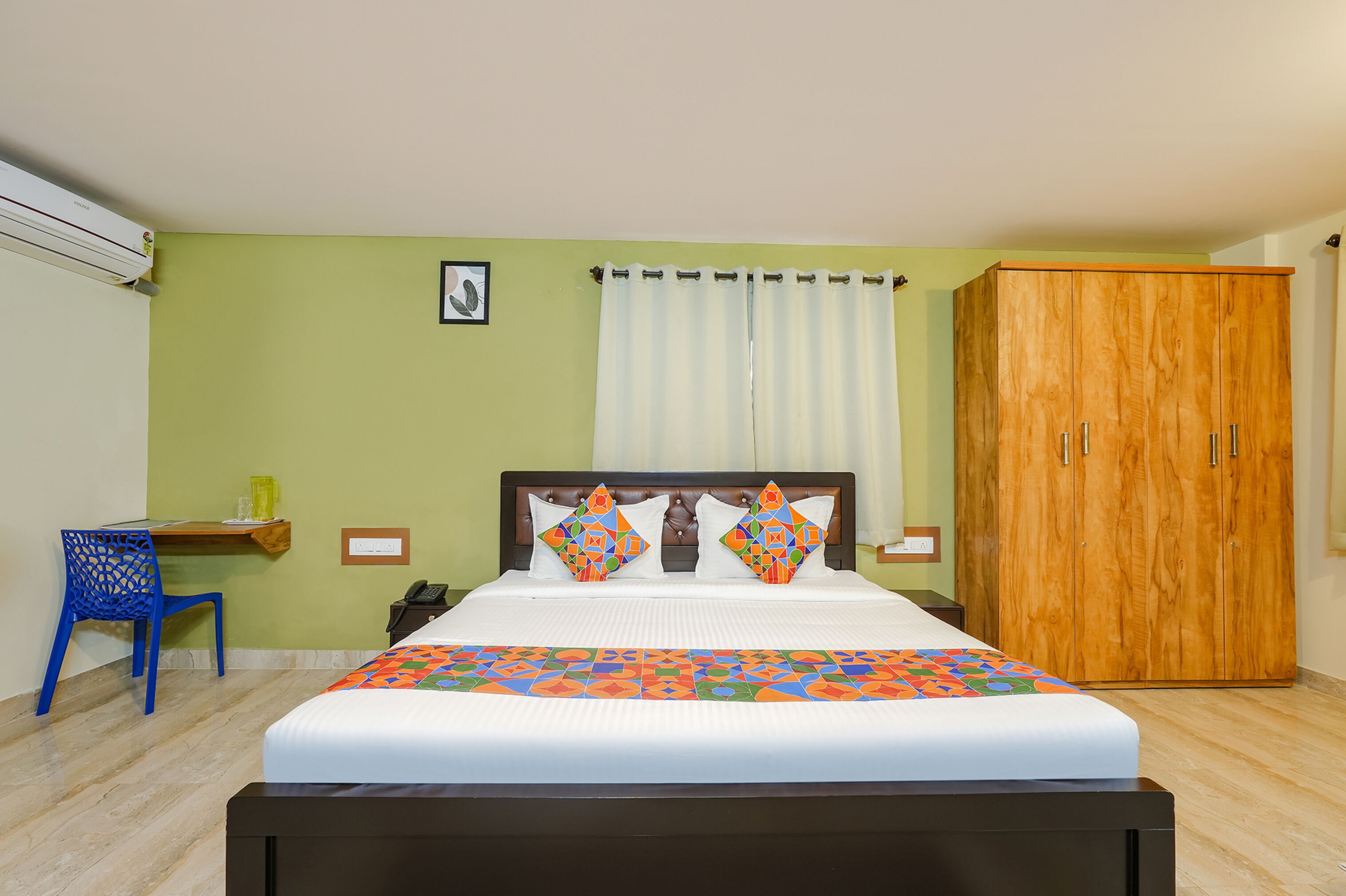 Um quarto bem arrumado com uma cama, um guarda-roupa de madeira, uma escrivaninha com cadeira e uma pequena prateleira.