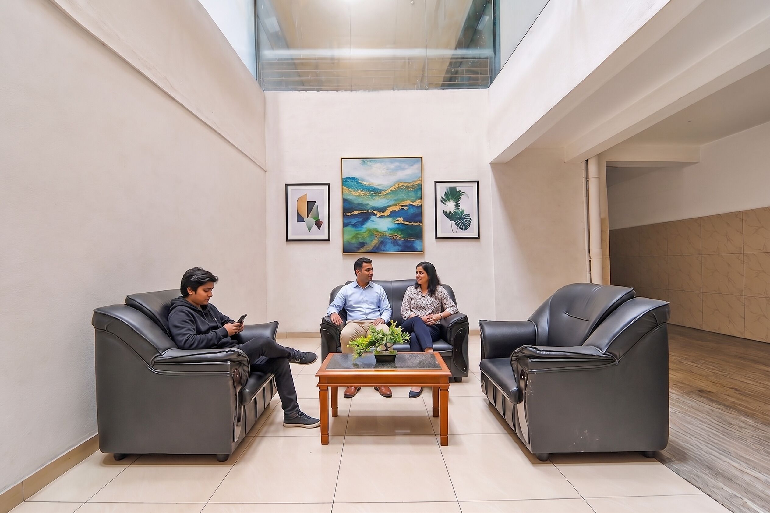 Um interior moderno com três poltronas de couro, uma mesa de centro de madeira e obras de arte nas paredes.