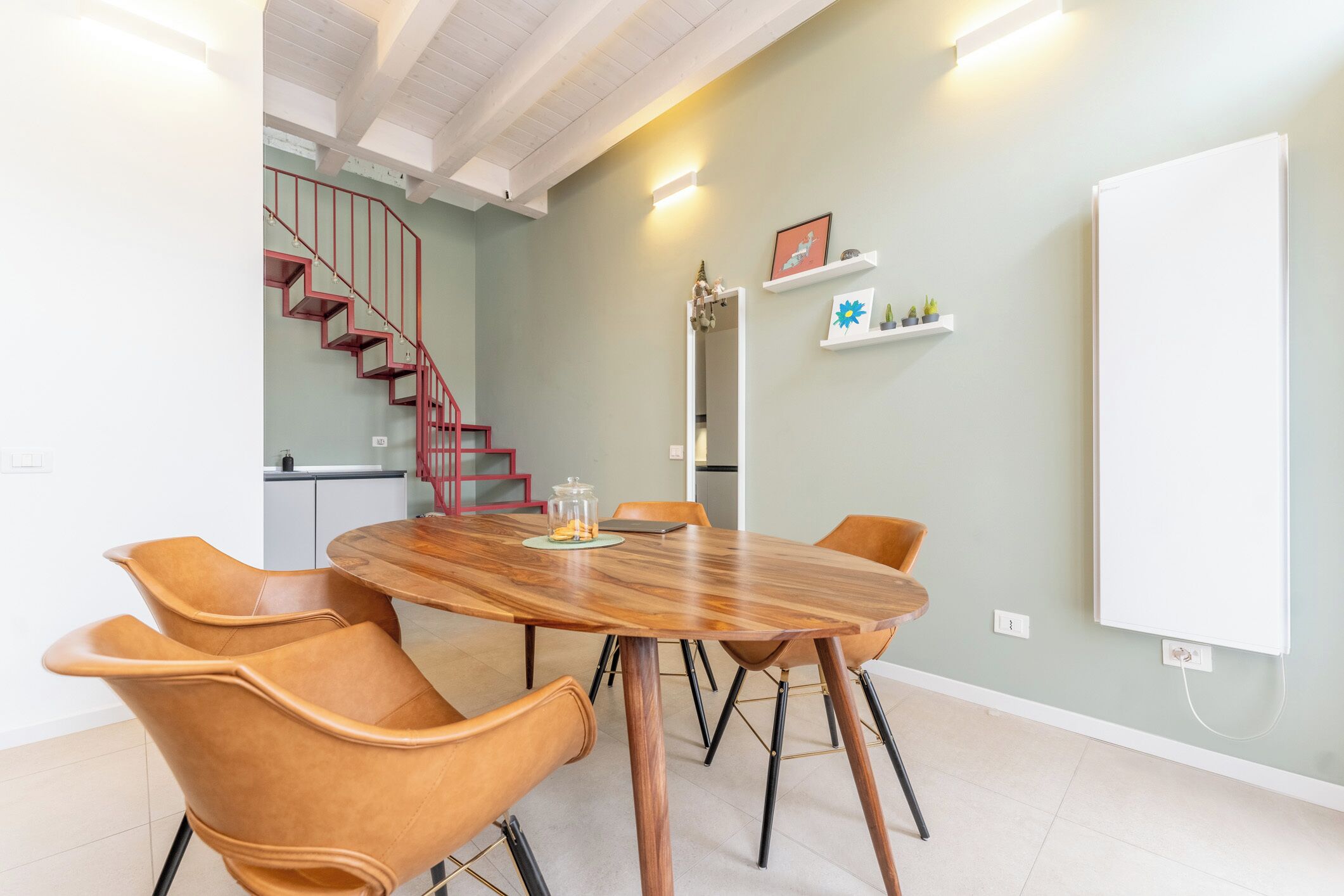 Uma sala de jantar com uma mesa de madeira e quatro cadeiras, uma escada com corrimãos vermelhos e uma lousa na parede.