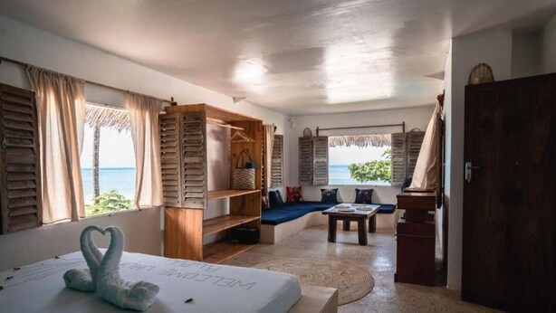 Quarto com cama, guarda-roupa de madeira, área de estar com vista para o mar e uma pequena mesa.