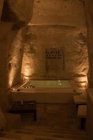 Um banho interno de pedra com uma banheira, uma mesinha e um banco.