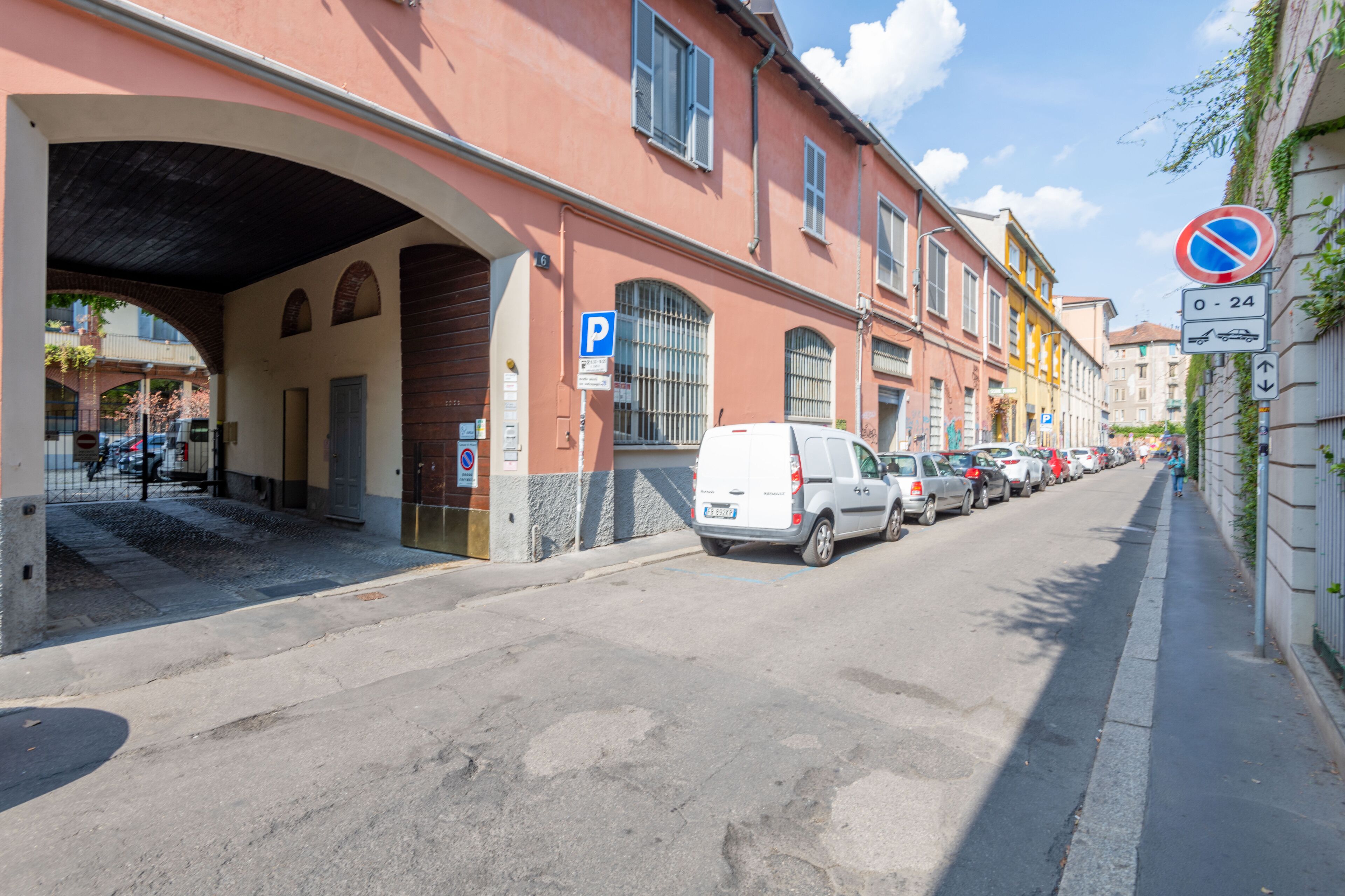 Rua com carros estacionados e um edifício com placa de estacionamento.