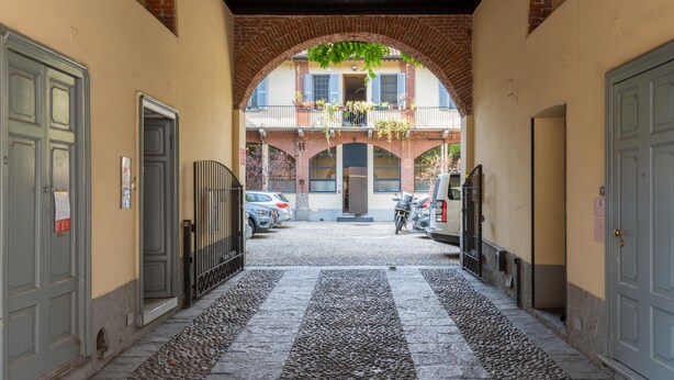 Uma passarela coberta para pedestres com piso de paralelepípedos, ladeada por edifícios com portas em arco e fachada de tijolos.