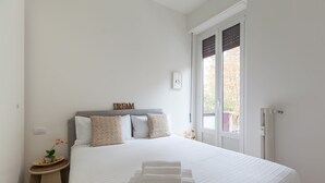 Cama bem arrumada com cabeceira rotulada "DREAM" em quarto claro com uma janela grande, mesa de cabeceira com uma pequena planta e radiador.