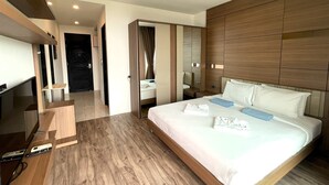 Quarto de hotel moderno com uma cama grande, piso de madeira, televisão e espelho.