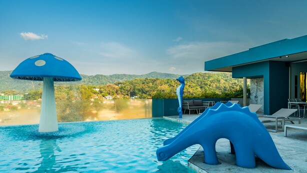 Uma piscina com uma fonte em formato de cogumelo azul e uma escultura de dinossauro azul.