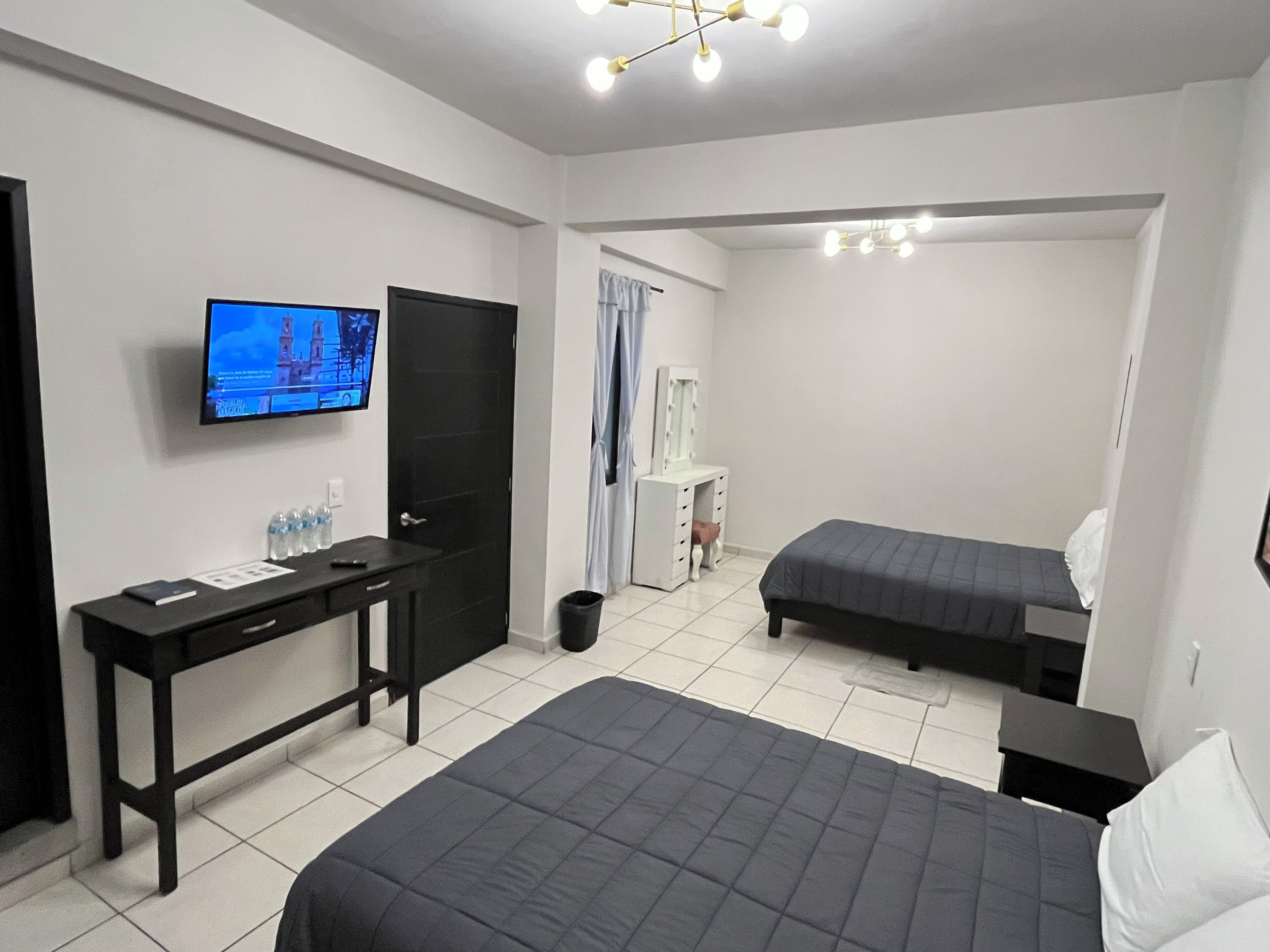 Quarto de hotel com duas camas, uma escrivaninha, televisão e toucador com iluminação.