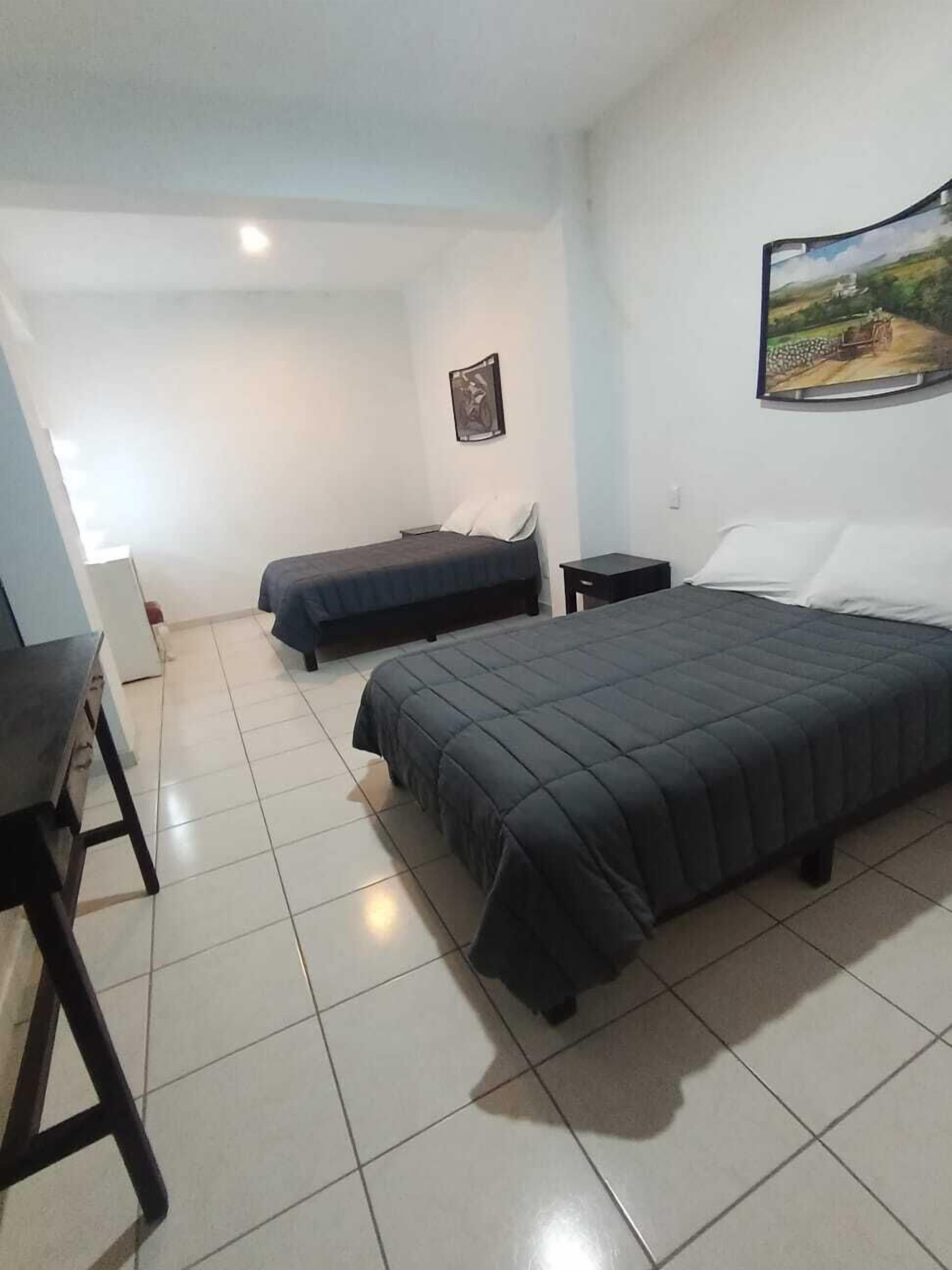 Quarto com duas camas, uma escrivaninha e um quadro na parede.