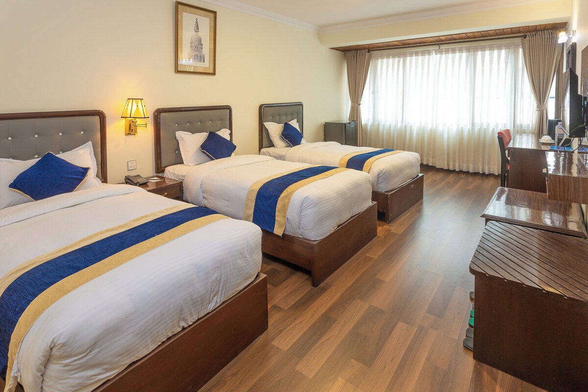 Quarto de hotel com três camas, soalho de madeira, secretária e televisão.