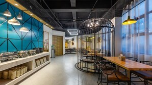 Um café moderno com área de estar central, um balcão de buffet à esquerda e grandes janelas à direita.