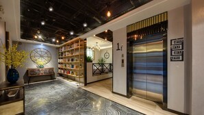 Um hall moderno com piso de mármore, um relógio grande, uma estante de livros e um elevador.
