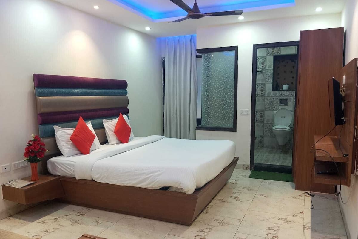 Quarto moderno com uma cama grande, uma mesa de cabeceira, um vaso de flores e um banheiro visível através de uma porta aberta.