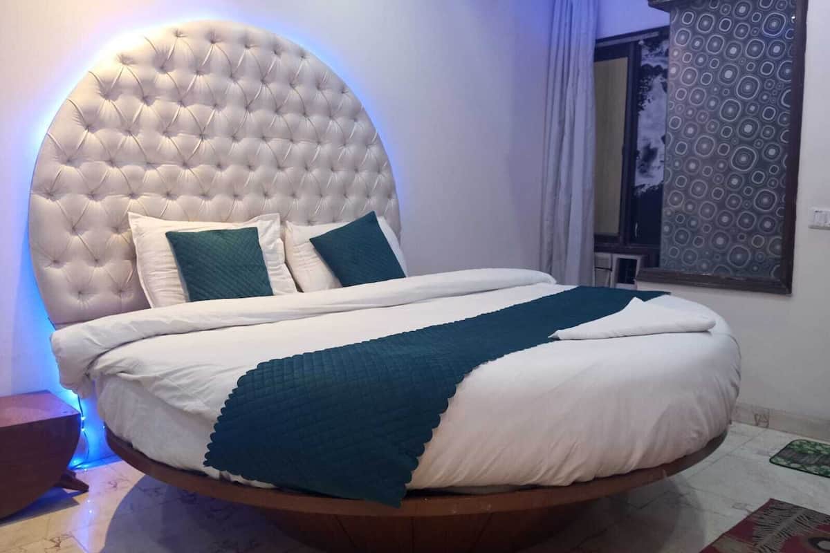 Uma cama redonda com cabeceira estofada, roupa de cama branca e almofadas decorativas verde-água.