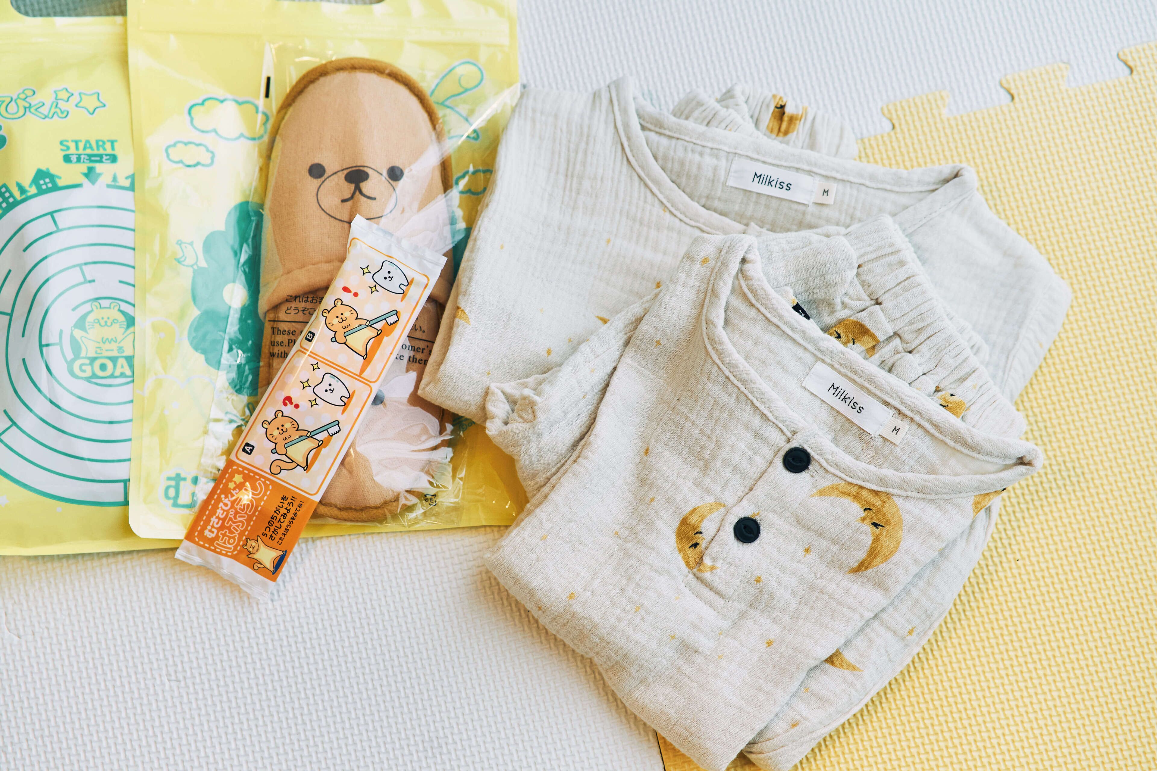 Um conjunto de roupa de bebé com motivos de lua e urso, uma bolsa amarela com ilustração de urso e uma etiqueta com padrão de urso e lua.