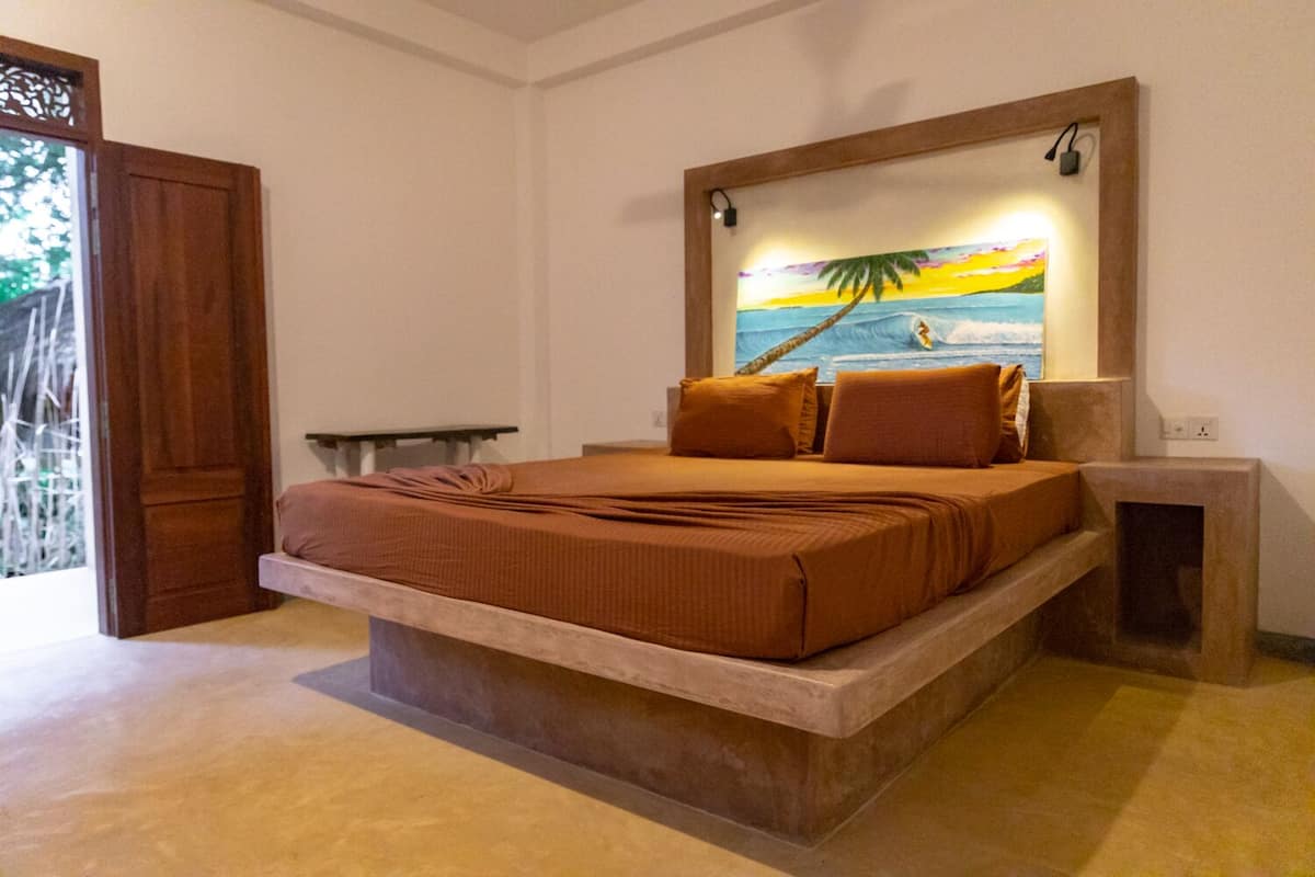 Quarto com cama no centro de uma plataforma, cabeceira de madeira com pintura, mesa de cabeceira e porta que dá para o exterior.