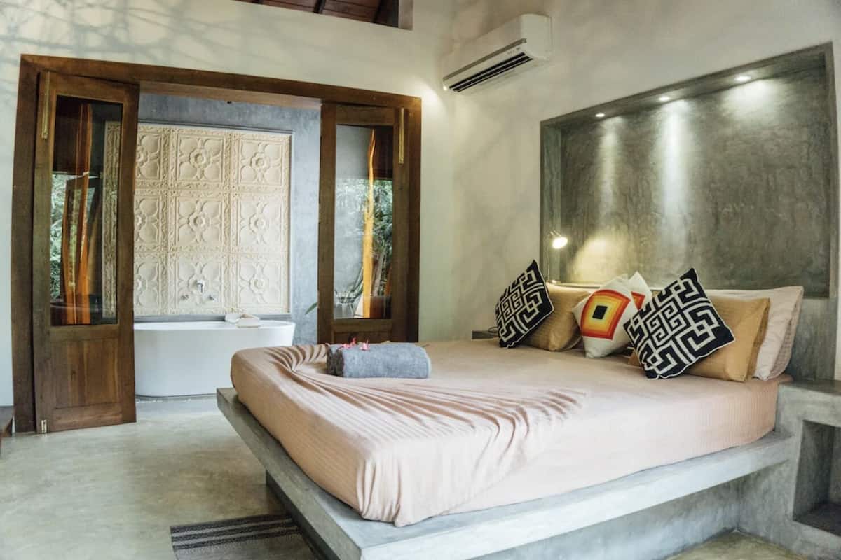 Quarto com uma cama grande, porta de madeira, banheira e ar condicionado fixado na parede.