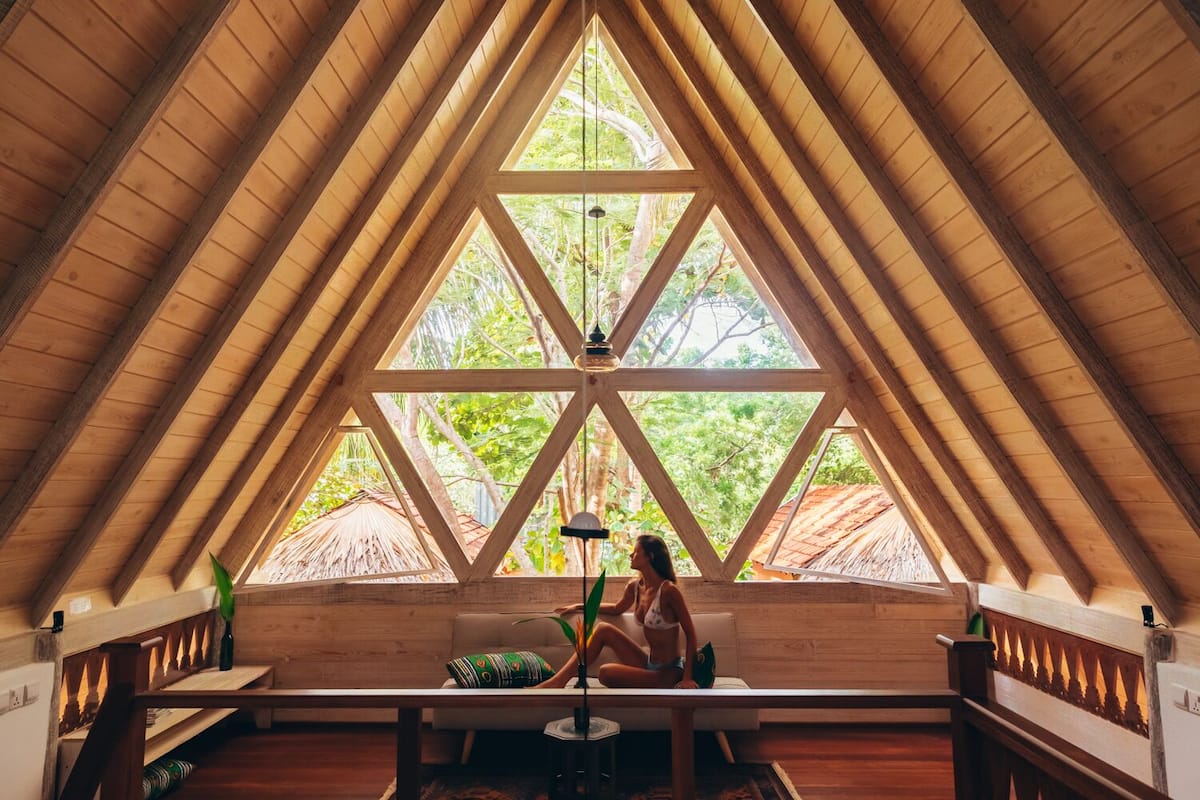 Quarto com teto de madeira alto e triangular, e grandes janelas.