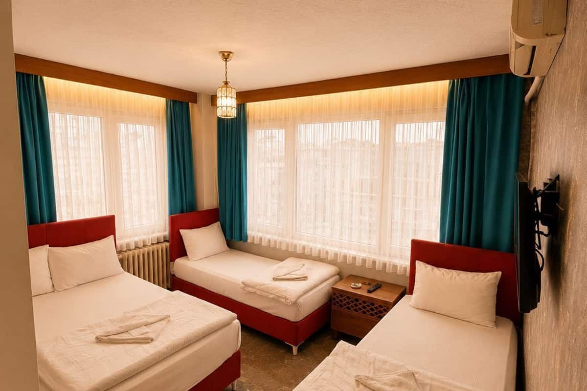 Quarto de hotel com três camas, uma cabeceira de madeira, uma mesinha e um ar-condicionado fixado na parede.
