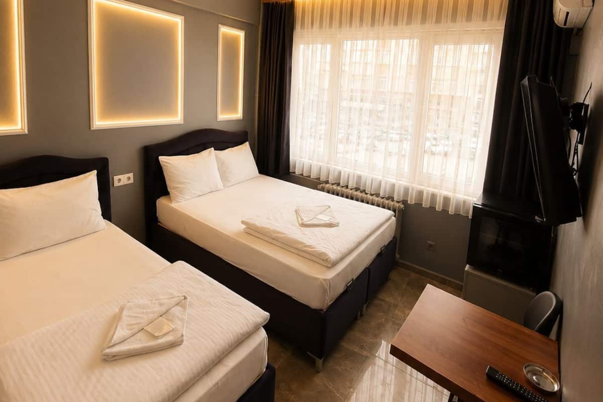 Quarto de hotel com duas camas, uma escrivaninha, uma cadeira e uma televisão.