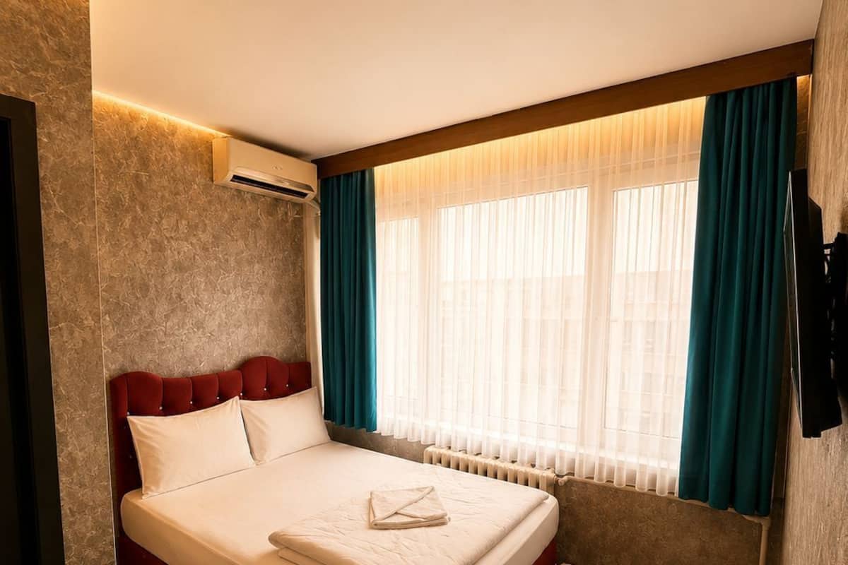 Quarto de hotel com uma cama, uma mesinha com um controle remoto e uma televisão fixada na parede.
