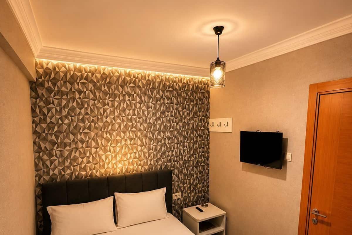 Quarto de hotel com cama, mesa de cabeceira, televisão e porta de madeira.