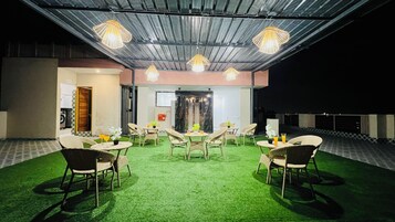 Pátio externo com grama sintética, móveis de vime e iluminação pendente.