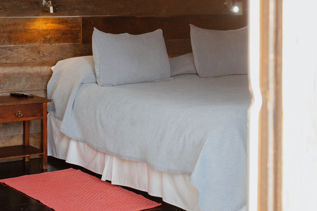 Quarto com cama, mesa de cabeceira, tapete vermelho e cabeceira de madeira.
