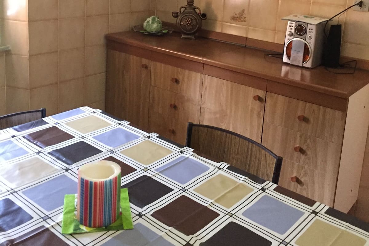 Cozinha com armários de madeira, painel de azulejos e uma mesa com toalha estampada.