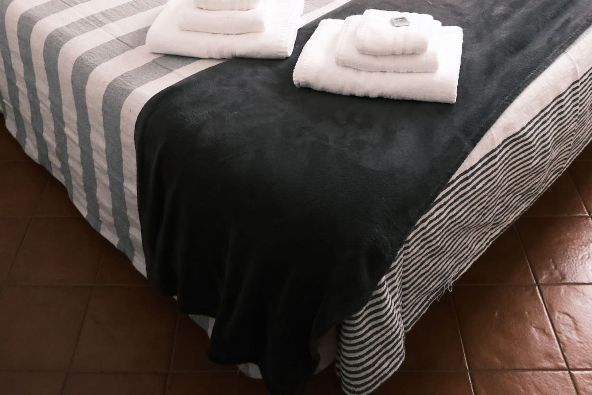 Cama bem arrumada com roupa de cama listrada e duas toalhas dobradas.