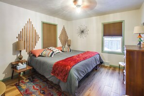 Quarto com cama, mesa de cabeceira, abajur, janela com persianas e um objeto decorativo na parede.