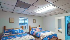 Quarto com duas camas, cada uma com colcha azul e branca, e uma janela com persianas.