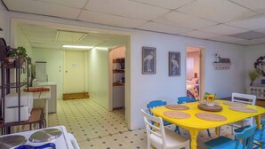 Uma sala de jantar com mesa amarela, cadeiras azuis e teto branco.
