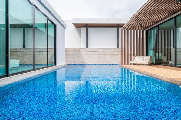 Piscina interior moderna com paredes de vidro transparente, deck de madeira e design minimalista.