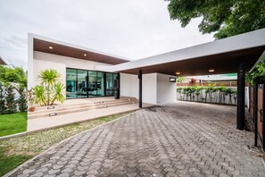 Um edifício moderno com entrada coberta, portas de vidro e área pavimentada com plantas em vasos.