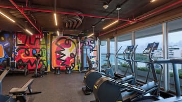 Uma academia com equipamentos de ginástica, uma janela ampla com vista e grafites coloridos nas paredes.