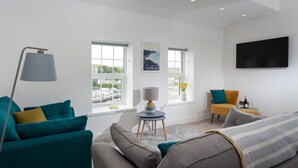 Uma sala de estar moderna com sofás verde-água e cinza, uma luminária de chão e uma TV de tela plana na parede.