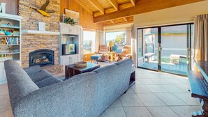 Uma sala de estar moderna com lareira de pedra, um sofá modular cinzento grande e uma varanda com móveis de exterior.