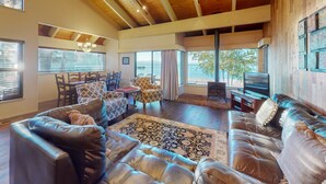 Uma sala de estar espaçosa com um sofá de couro grande, tapete estampado, vigas de madeira no teto e vista para o exterior.